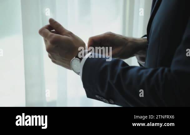 Close-up of a successful man is putting on a watch near the window ...