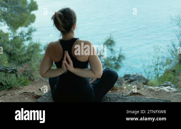 Woman sitting on the beach and holding hands in namaste pose behind ...