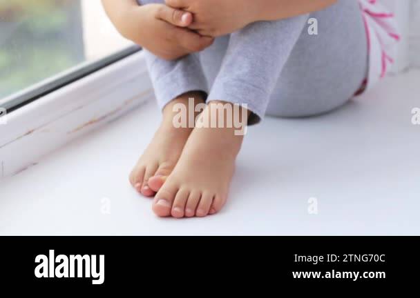 Close up of hands on knees of cute little girl sitting on windowsill of ...