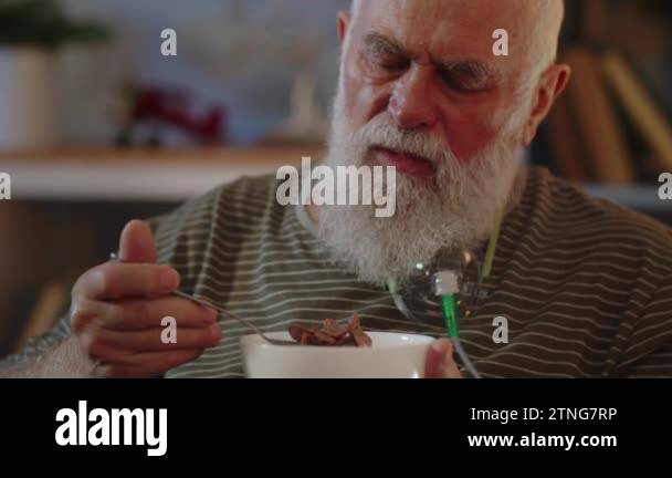 Old man with breathing mask stay in chair and eat food. Have dinner ...