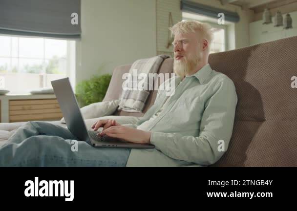 Serious albino man with white thick beard typing on laptop, sitting on ...
