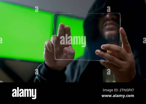 Hacker using clear glass tablet with green screen monitor behind and ...