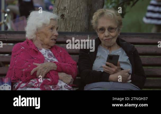 Two old women are talking. Retired people sitting on the bench in the ...