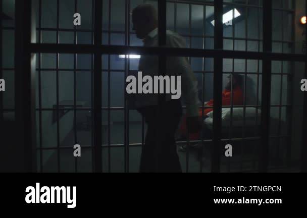 Prison officer with police baton watches criminals in prison cells ...