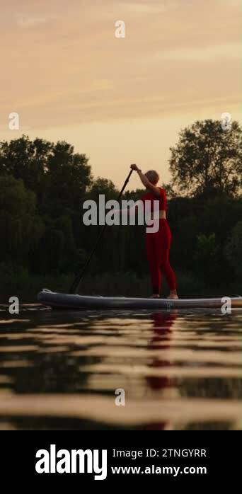 Vertical Screen: Fit woman paddling on SUP board along river bank ...