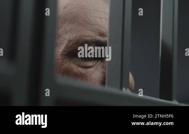 Face close up of angry elderly prisoner standing behind metal bars in ...