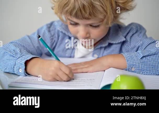 Elementary school student boy or girl writing letters, studying at desk ...