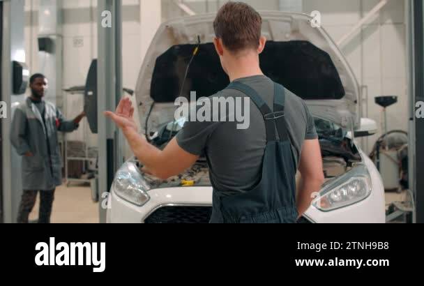 two diverse international auto mechanics, masters working underneath car lifting machine at the ...