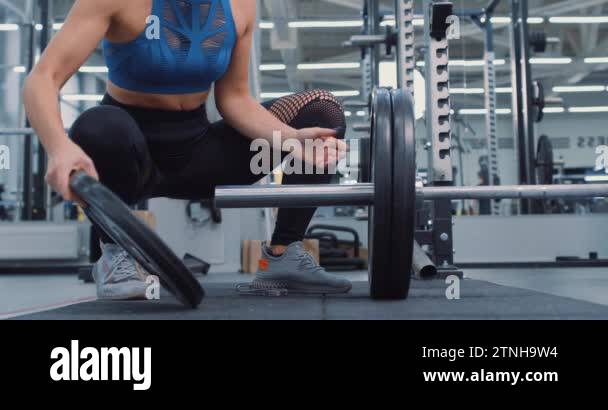 Fitness girl adding weights to the barbell for dead lift training ...