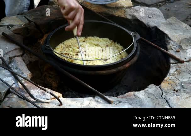 Uzbek national dish pilaf in a large cast-iron cauldron on the fire ...