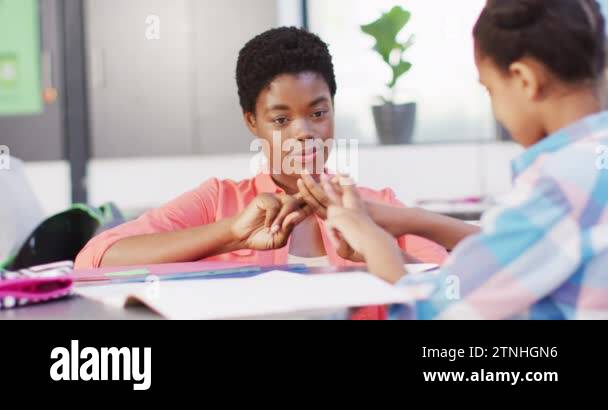 Diverse female teacher and happy schoolchildren at desks learning sign ...