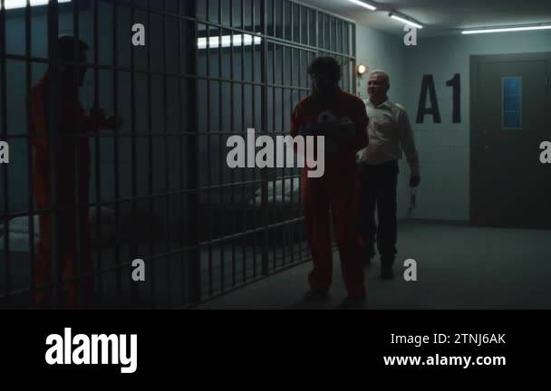 Prison employee locks criminal in orange uniform in jail cell. Prisoner ...