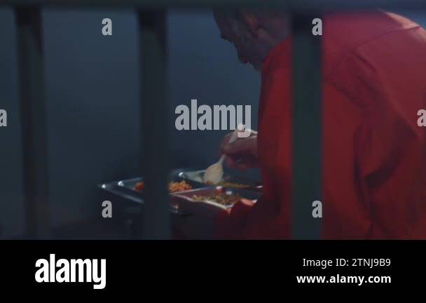 Close up of elderly prisoner in orange uniform sitting in prison cell ...