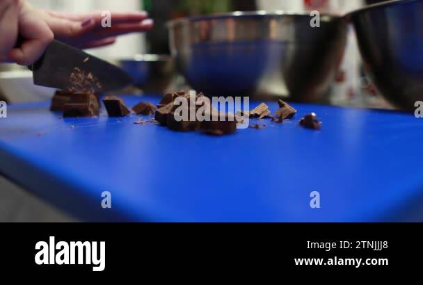 Women's hands cut chocolate with a knife, grinding it to prepare a ...