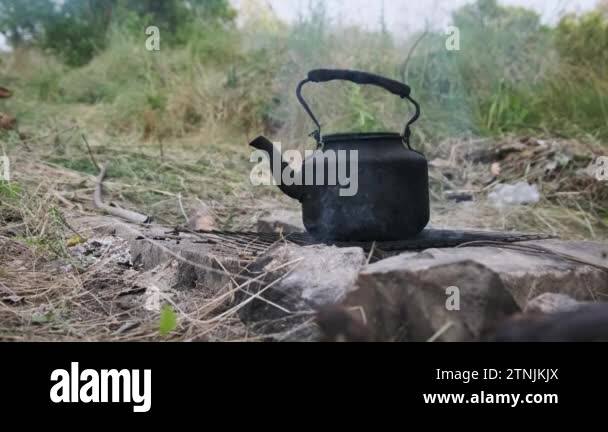 Old kettle standing on a tourist campfire in nature. Blackened with ...