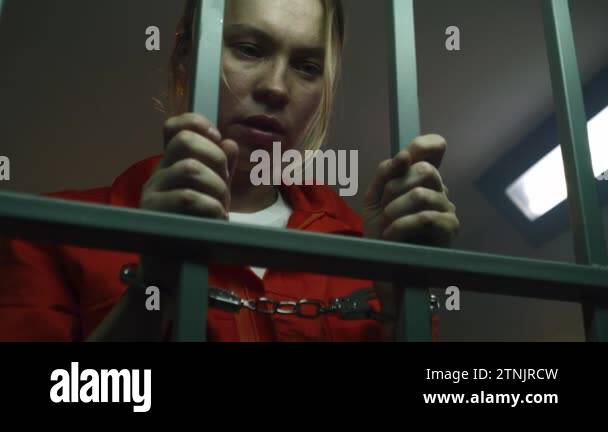 Female prisoner in orange uniform stands in prison cell. Scared woman ...
