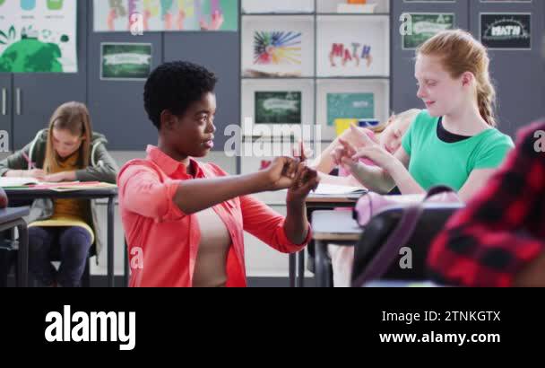 Diverse female teacher and happy schoolchildren at desks learning sign ...