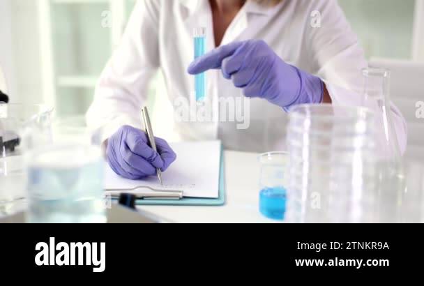 Scientist holds test-tube with examined blue reagent writing down ...