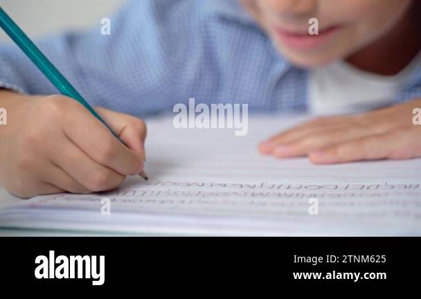 Elementary school student boy or girl writing letters, studying at desk ...