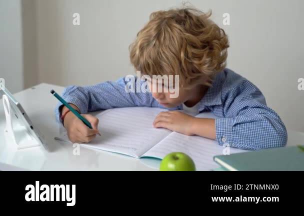 Elementary school student boy or girl writing letters, studying at desk ...