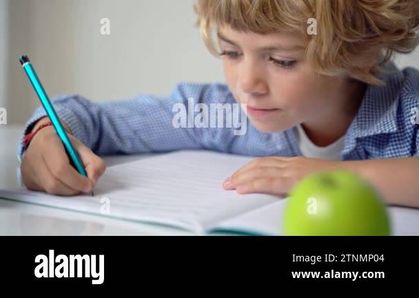 Elementary school student boy or girl writing letters, studying at desk ...