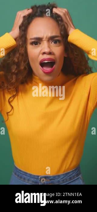 Frustrated and angry young woman tears hair out - green studio ...