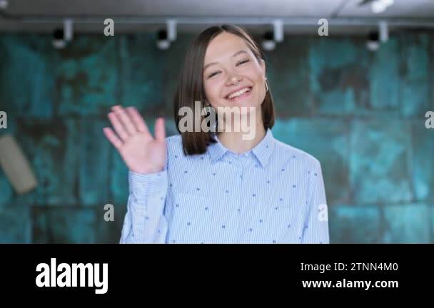 Young smiling cheerful woman looking at camera waving her hand while ...
