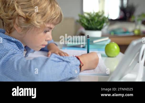 Elementary school student boy or girl writing letters, studying at desk ...