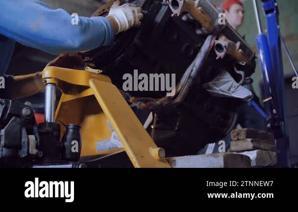 Two mechanics with the help of a crane load an automobile engine onto a ...