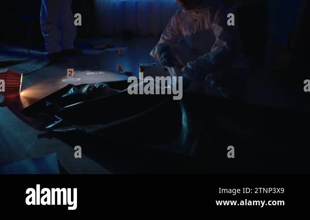 A team of forensic experts work at a crime scene in a dark apartment ...