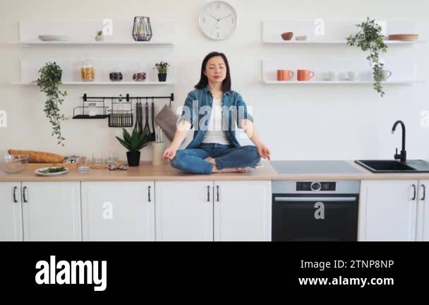 Cheerful asian female in casual clothes and glasses relaxing in lotus ...