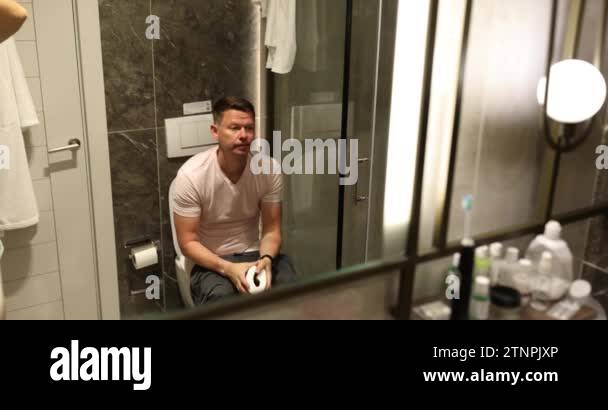 Young man sits at home on toilet bored. Sad man sits on toilet with ...