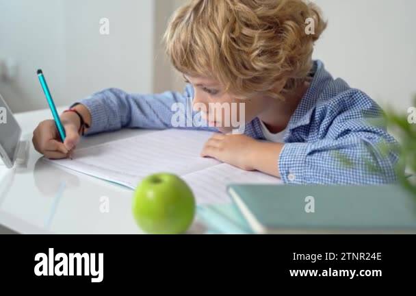 Elementary school student boy or girl writing letters, studying at desk ...
