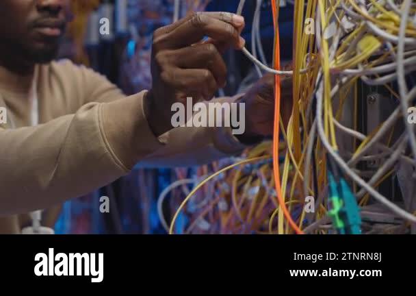 Cropped shot of Black IT engineer connecting tangled server wires in operational rack server ...