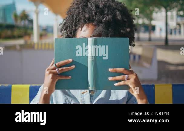 Young girl peeping from book sitting at sunny street closeup. Portrait ...