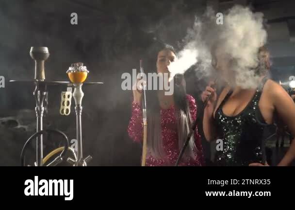 Two beautiful girlfriends are having fun and smoking the hookah in the ...