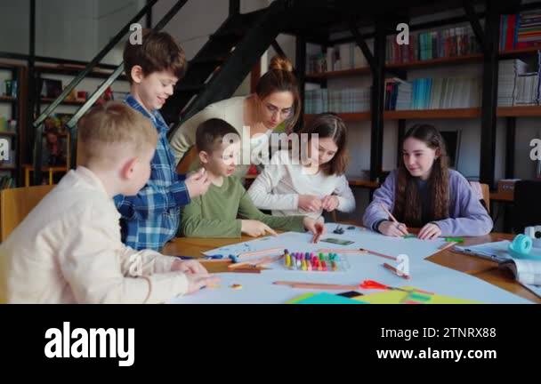 Positive teacher looks at drawings and plasticine figures that children ...