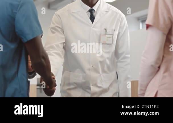 Tilt up shot of team of diverse doctors with nurses shaking hands while ...