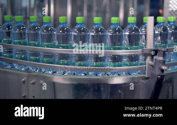 Filled, capped and clean bottles slowly move on a curved factory line ...