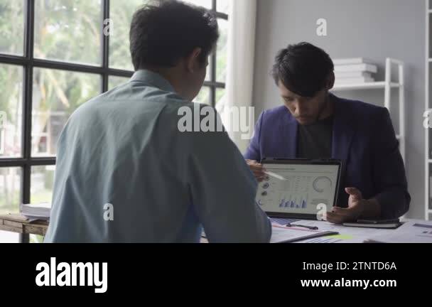 Two young asian businessmen in suits discussing financial market data ...