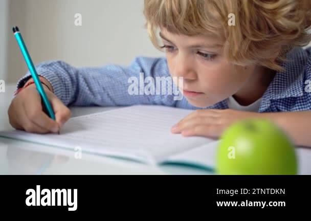 Elementary school student boy or girl writing letters, studying at desk ...