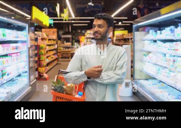 Smiling indian man walking in aisle with his trolely at supermarket ...