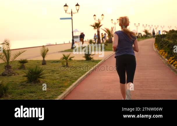 Road runner woman running in park, jogging along the palm grove ...