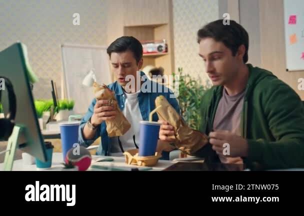 Working businessmen eating sandwiches talking at workplace close up ...