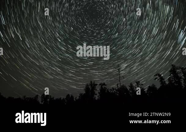 Time lapse of comet-shaped star trails over the forest in the night sky ...
