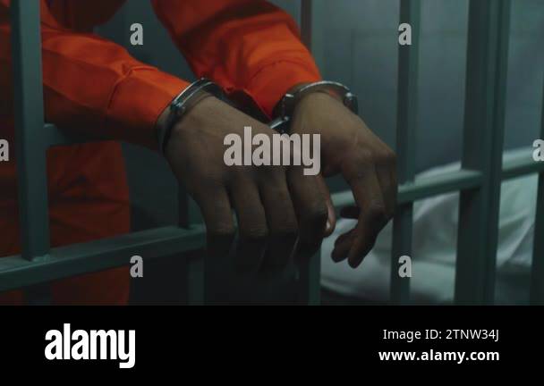 Close up shot of hands in handcuffs leaning on prison cell bars ...
