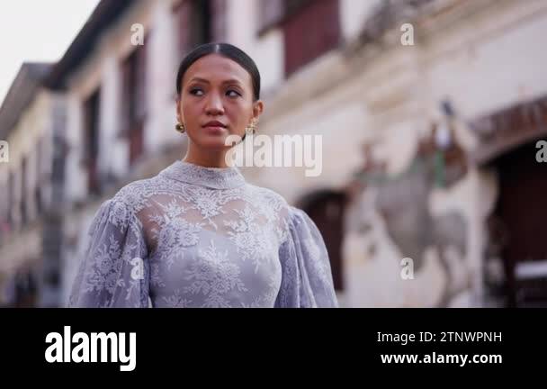 A woman sporting a chic bun hairstyle and dressed in a lilac gown walking in the historical ...