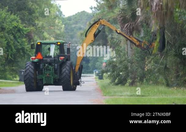 Public works utility tractor pruning trees and greenery braches on ...