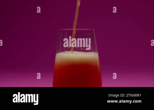 Super slow motion of pouring orange juice into glass. Placed on pink ...