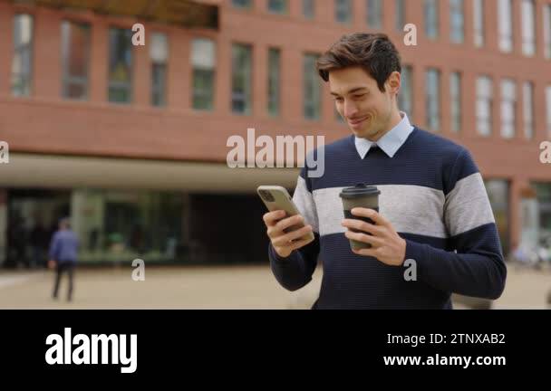 Young Guy Standing near Offcie Building Typing Messages on Smartphone and Holding Coffee. Man ...